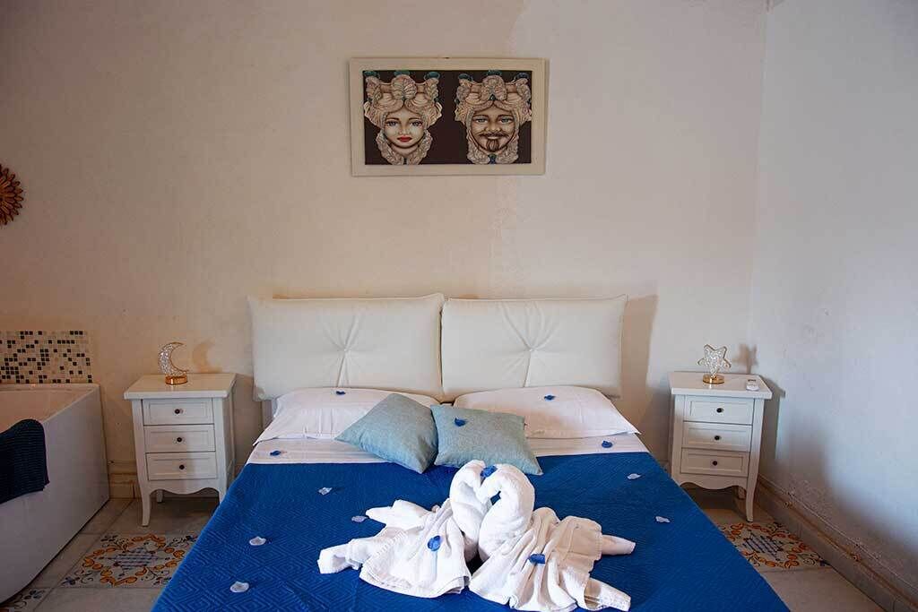 Quarto com cama, duas mesas de cabeceira, cabeceira branca e um quadro na parede.