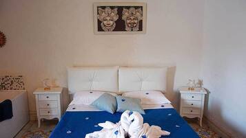 Quarto com cama, duas mesas de cabeceira, cabeceira branca e um quadro na parede.