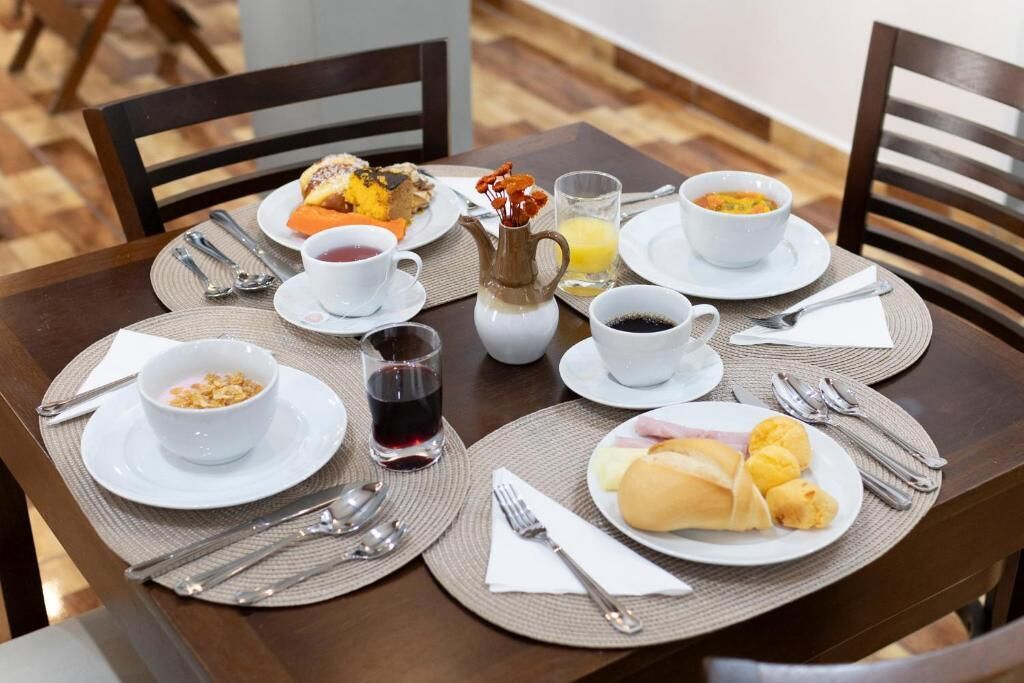 Mesa de café da manhã posta com pratos de comida, xícaras e um jarro.