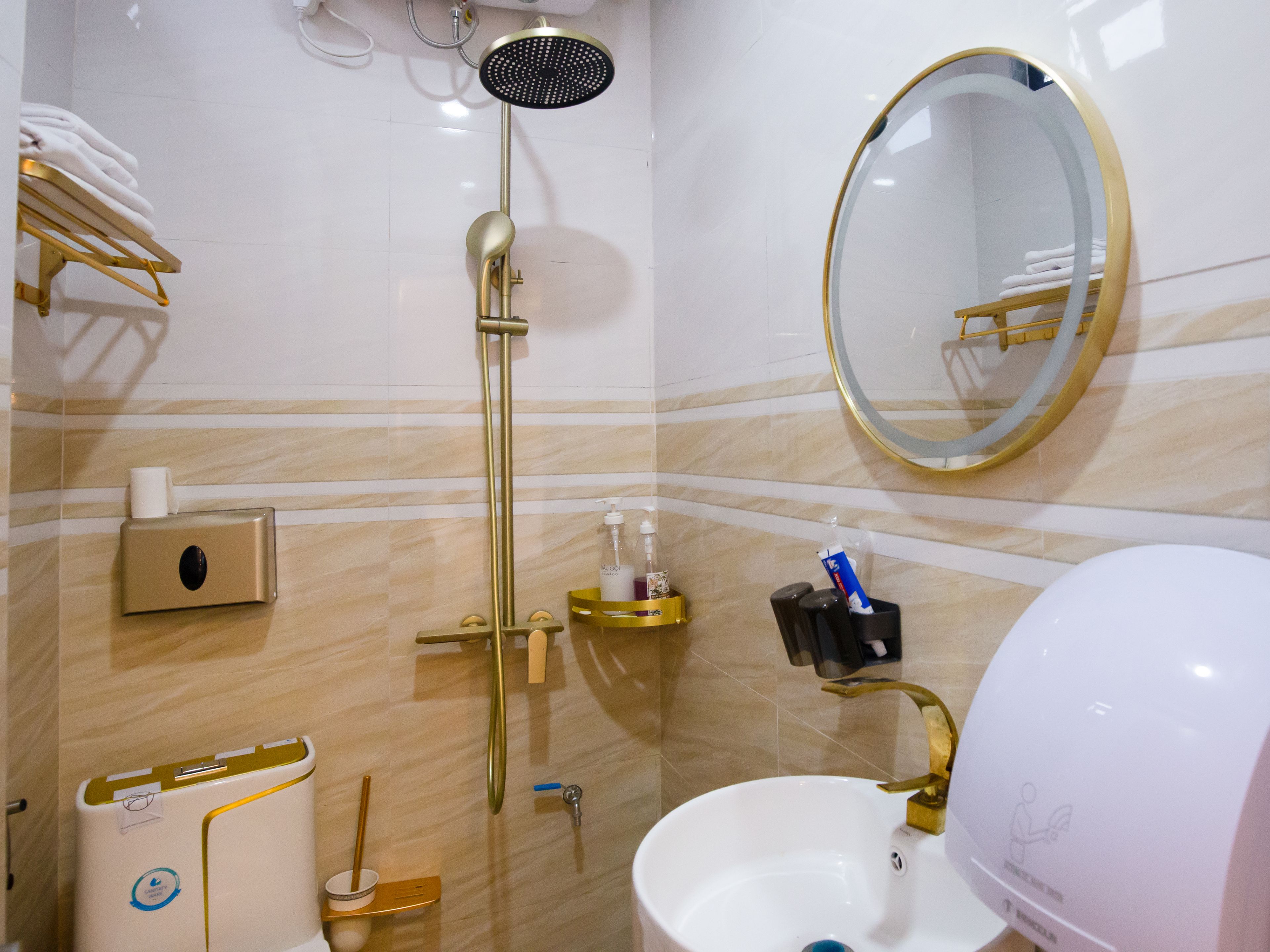 Um banheiro com chuveiro dourado, pia branca, espelho e porta-toalhas.