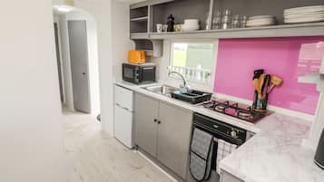 Uma cozinha compacta com micro-ondas, torradeira, pia e escorredor de louça.