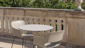 Um terraço com uma mesa redonda e duas cadeiras, um corrimão e uma palmeira ao fundo.