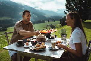 Um casal jantando ao ar livre, com uma mesa posta para refeição, emoldurado por uma paisagem deslumbrante.