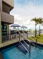 Área da piscina com degraus de acesso, assentos externos e guarda-sóis.
