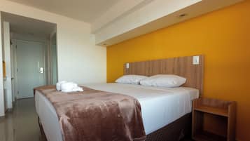 Quarto de hotel com cama, cabeceira de madeira, manta marrom e toalha branca.