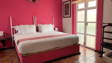 Quarto com cama grande, mesa de cabeceira de madeira, luminária na parede e janela com vista.