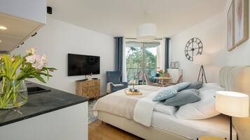 Quarto moderno com cama, mesa de cabeceira, televisão e vista para o exterior.