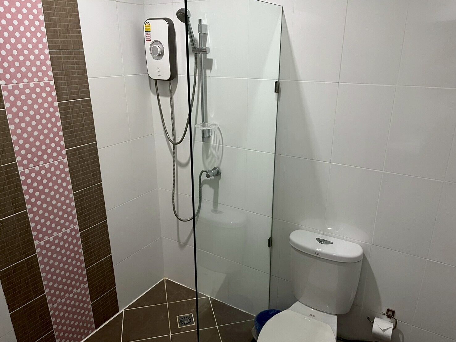 Uma casa de banho com chuveiro, sanita e termoacumulador de água na parede.