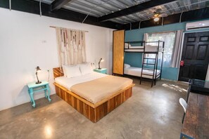 Quarto com cama de solteiro, estrutura de cama de madeira, mesa pequena com abajur e cortina.