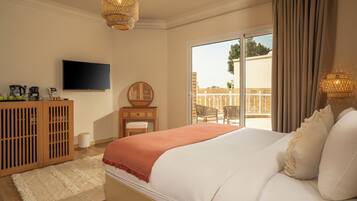 Quarto com cama grande, televisão, armário de madeira e varanda com cadeiras.