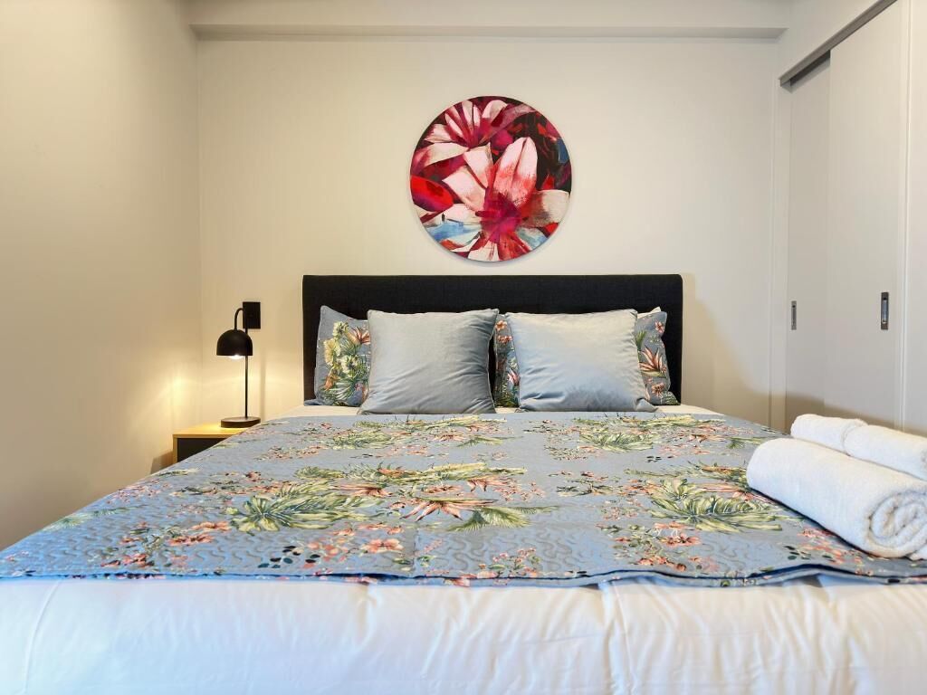 Quarto com cama, uma obra de arte circular na parede, mesa de cabeceira com abajur e uma toalha enrolada.
