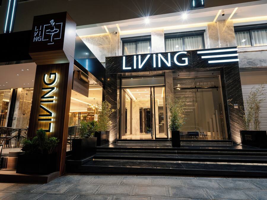 Entrada de hotel moderna com um letreiro grande 'LIVING', fachada de vidro e interior bem iluminado.