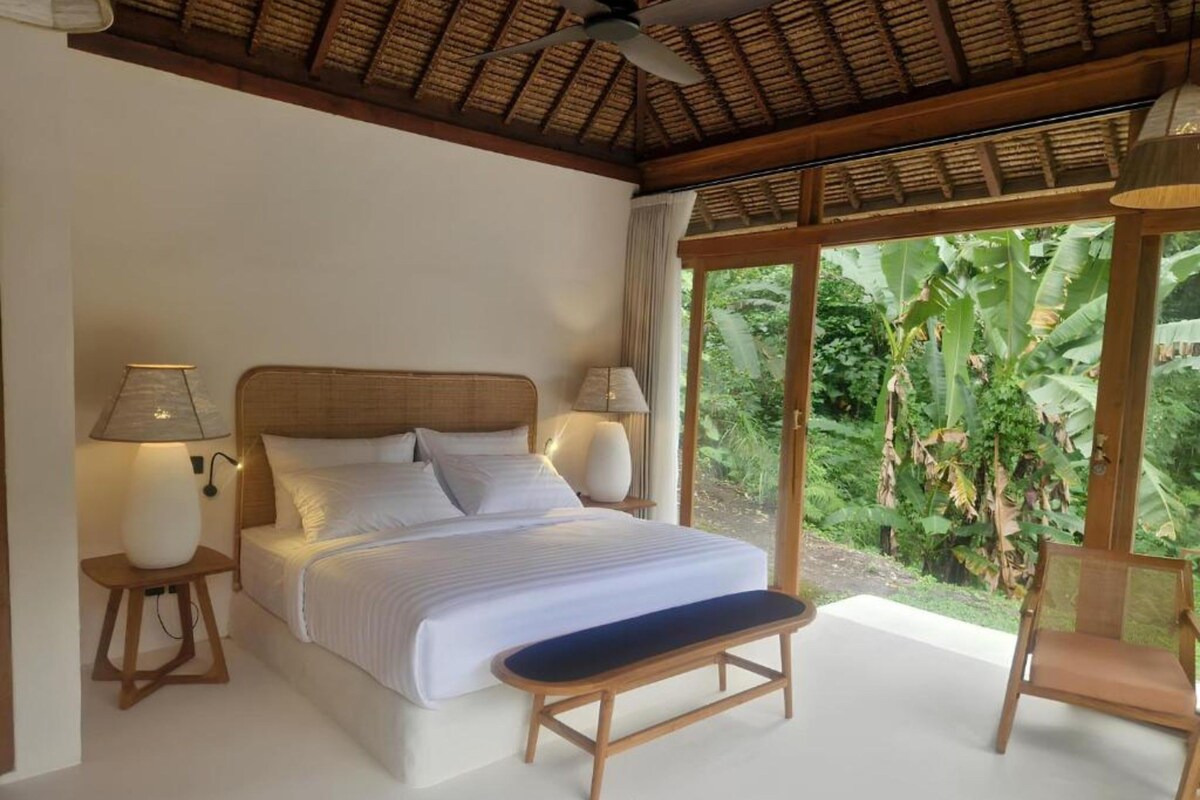 Um quarto com uma cama, abajures, um banquinho e uma cadeira.