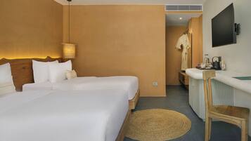 Quarto de hotel com duas camas, uma escrivaninha, uma cadeira, uma televisão e um banheiro visível ao fundo.