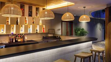 Uma área de bar com balcão, banquetas e luminárias pendentes.