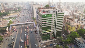 Um edifício de vários andares com uma placa grande de 'HOTEL' na fachada, um terraço no telhado e uma rua movimentada abaixo.