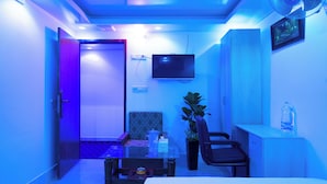 Quarto de hotel com cama, escrivaninha, cadeira, televisão e planta.