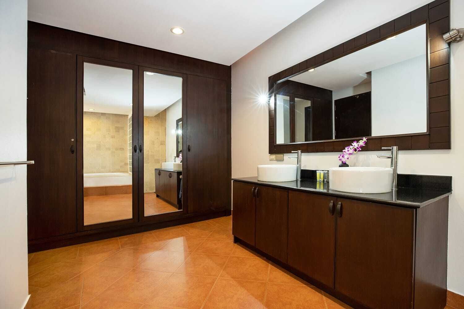 Casa de banho moderna com um espelho grande, duas pias e área de duche visível através de uma porta deslizante.