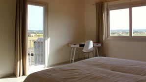 Quarto com uma cama, uma escrivaninha e uma cadeira. Há uma janela com vista para o campo.
