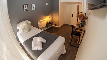 Quarto de hotel com cama, mesa de cabeceira, cadeira, escrivaninha com um laptop e televisão na parede.
