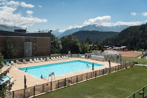 Piscina com cadeiras de sol e vista para montanhas.