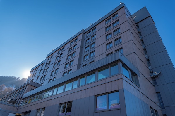 Um hotel com vários andares, design arquitetônico moderno, com grandes janelas e uma entrada de canto destacada.