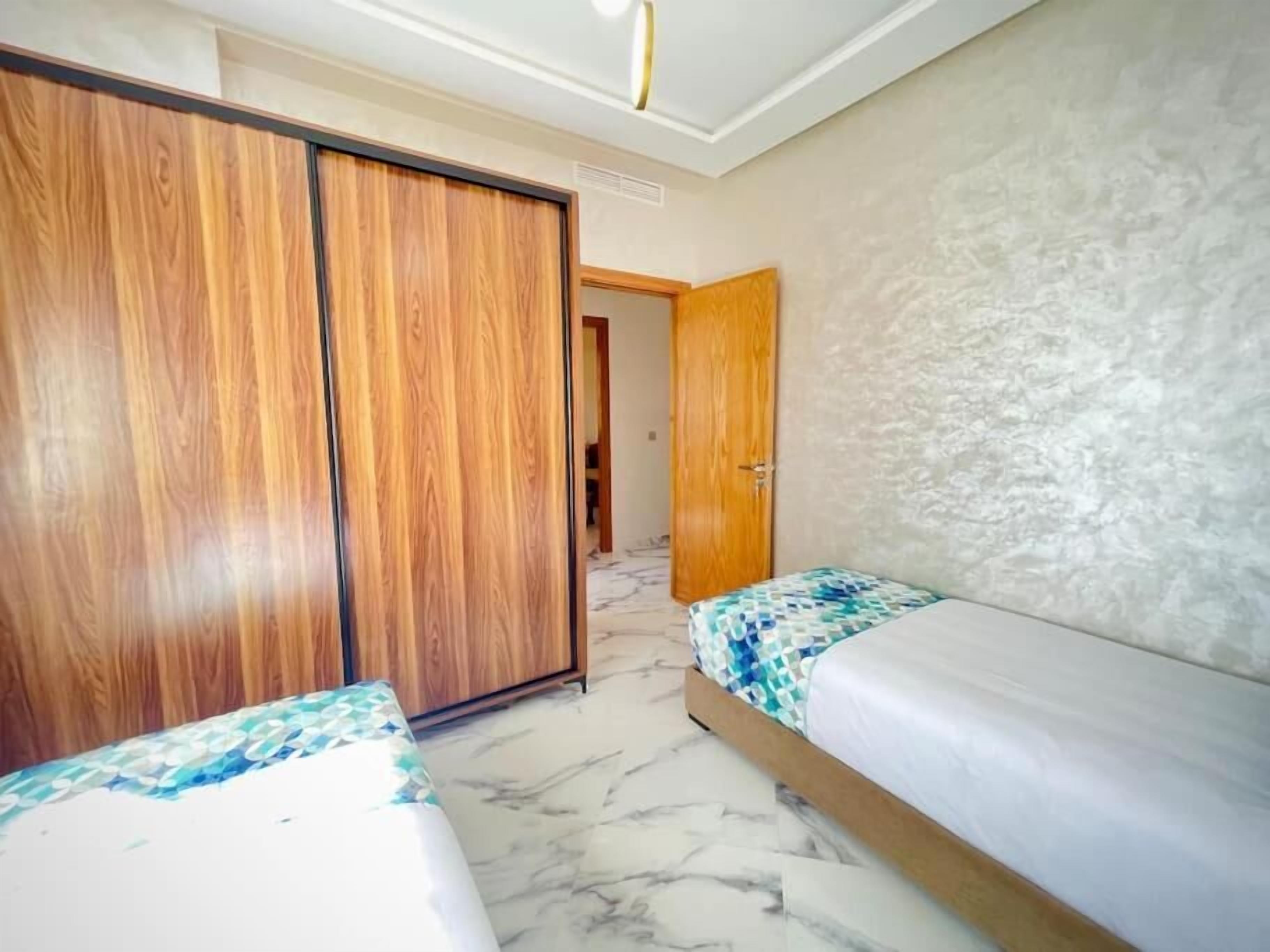 Quarto com duas camas de solteiro, guarda-roupa de madeira e parede texturizada.