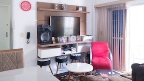 Sala de estar com televisão, ventilador de teto, uma cadeira vermelha e um sofá.