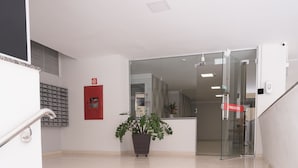 Um hall de entrada limpo e moderno, com uma escadaria de mármore, um balcão de recepção e um vaso de plantas.
