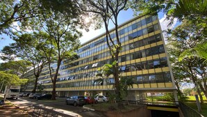 Um edifício de vários andares com fachada amarela e azul, rodeado por árvores e carros estacionados.