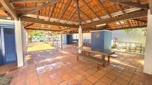 Um alpendre descoberto e coberto, com chão de azulejos, um banco e uma parede decorativa.