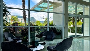 Um interior moderno com grandes janelas de vidro, duas poltronas escuras, uma pequena mesa redonda e um vaso com planta.