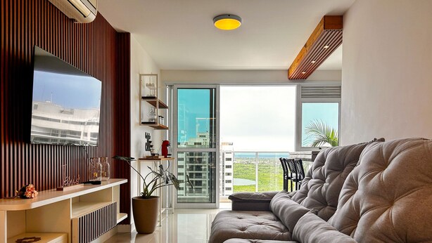 Uma sala de estar moderna com um sofá grande, uma TV de tela plana e uma varanda com vista para a cidade.
