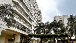 Um edifício moderno com várias varandas, um espelho d'água circular e palmeiras ao redor.