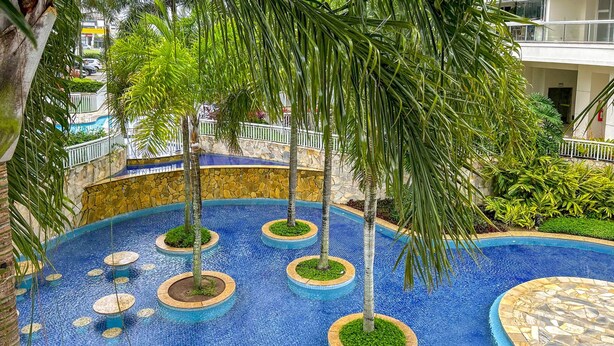 Piscina com plataformas circulares e palmeiras, cercada por um muro de pedra e uma varanda.