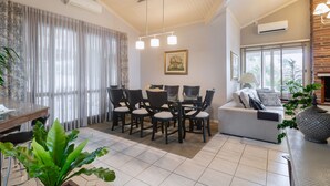 Uma sala de estar moderna com área de jantar, apresentando teto de madeira, uma janela grande com cortinas, um sofá e uma mesa de jantar com cadeiras.