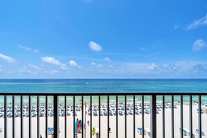 Vista da praia com guarda-corpo de varanda, guarda-sóis e cadeiras de praia.