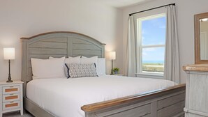 Quarto com cama grande, duas mesas de cabeceira, um criado-mudo, janela com cortinas e um espelho.