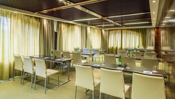 Uma sala de conferências com mesas e cadeiras, cortinas e iluminação no teto.