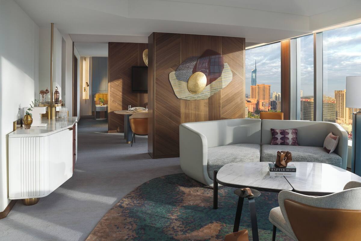 Quarto de hotel moderno com vista para a cidade, área de refeições e sala de estar com sofá e poltronas.