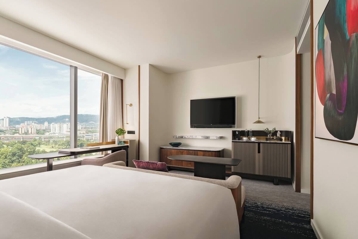 Quarto de hotel com uma cama grande, escrivaninha, televisão e vista para a cidade.