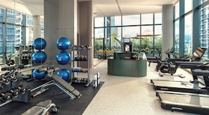 Uma academia moderna com diversos equipamentos de exercício, grandes janelas e vista para o verde lá fora.