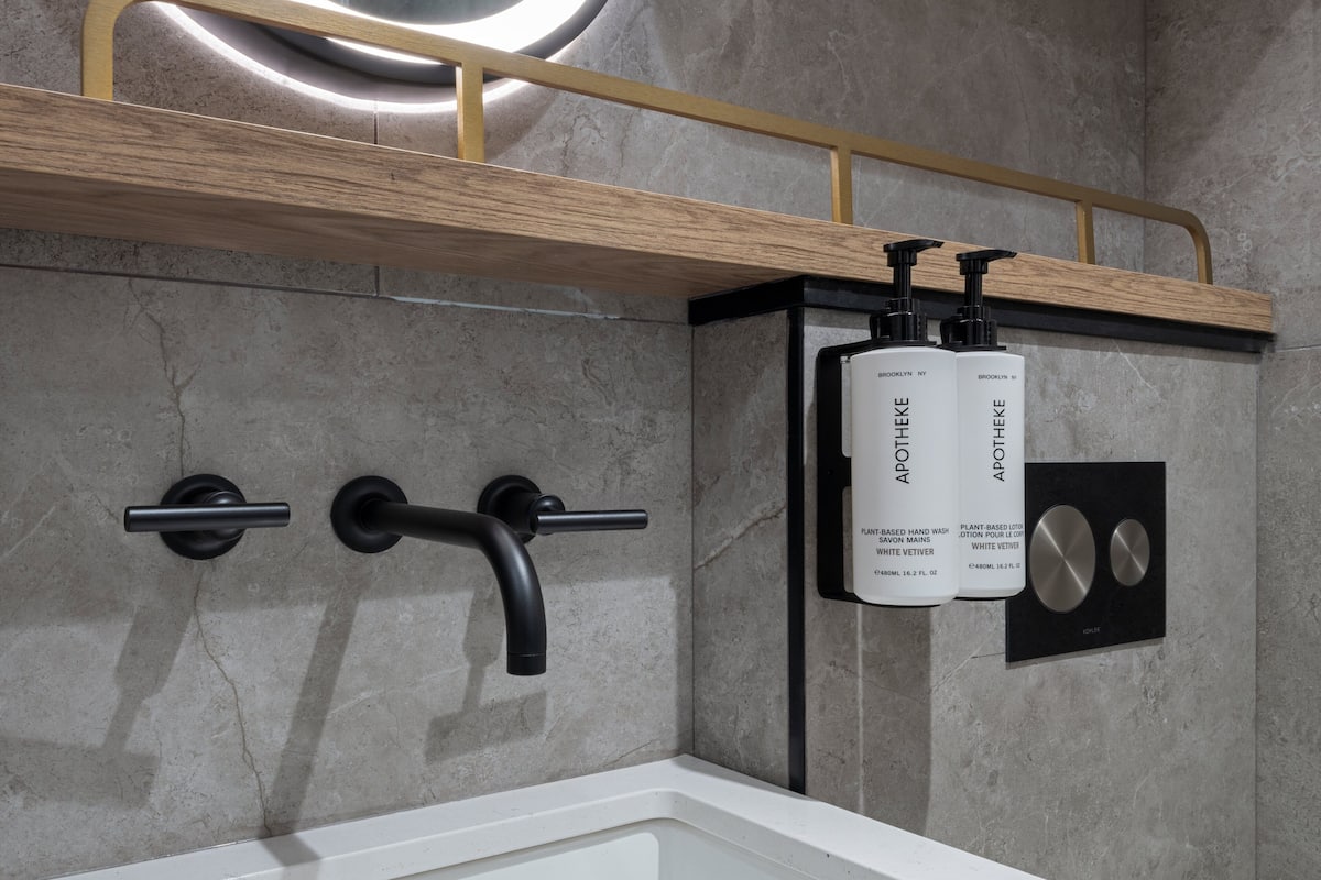Um banheiro com design moderno, com uma banheira, uma prateleira de madeira com dois frascos de sabonete líquido Apotheke e uma torneira preta.