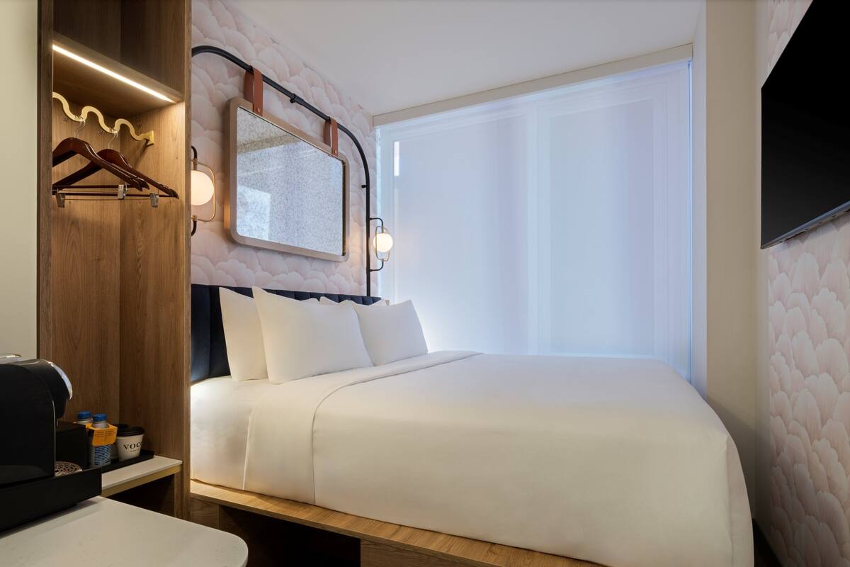 Quarto de hotel moderno com uma cama grande, uma escrivaninha de madeira, um espelho e uma televisão fixada na parede.