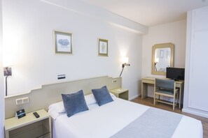 Quarto de hotel com uma cama, mesas de cabeceira, escrivaninha com cadeira, espelho e televisão.