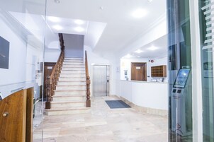Um hall de hotel com uma escadaria de mármore, um balcão de recepção e um painel de vidro.