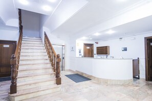 Um hall de hotel com escadaria de mármore, balcão de recepção e porta de uma sala privativa.
