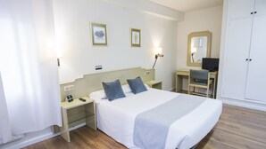 Quarto de hotel com cama, mesas de cabeceira, escrivaninha com cadeira, guarda-roupa e duas quadros na parede.