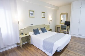 Quarto de hotel com cama, mesas de cabeceira, escrivaninha com cadeira, guarda-roupa e duas quadros na parede.