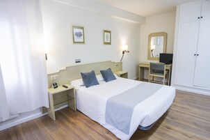Quarto de hotel com cama, mesas de cabeceira, escrivaninha com cadeira, guarda-roupa e duas quadros na parede.